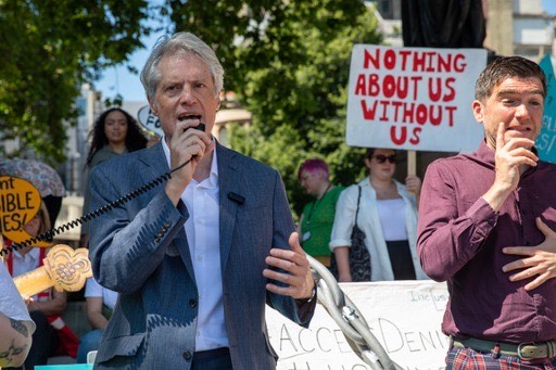 Ben Coleman MP speaking at the protest. A BSL interpreter is signing ...